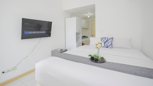 Quarto de hotel moderno com uma cama, uma TV fixada na parede e uma mesinha de cabeceira.