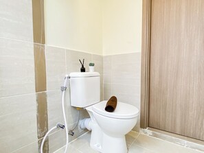 Sanitário com vaso branco, toalha marrom no assento, uma pequena garrafa preta e um recipiente branco na caixa acoplada.
