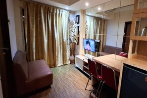 Um espaço compacto com sofá, escrivaninha, computador e televisão.