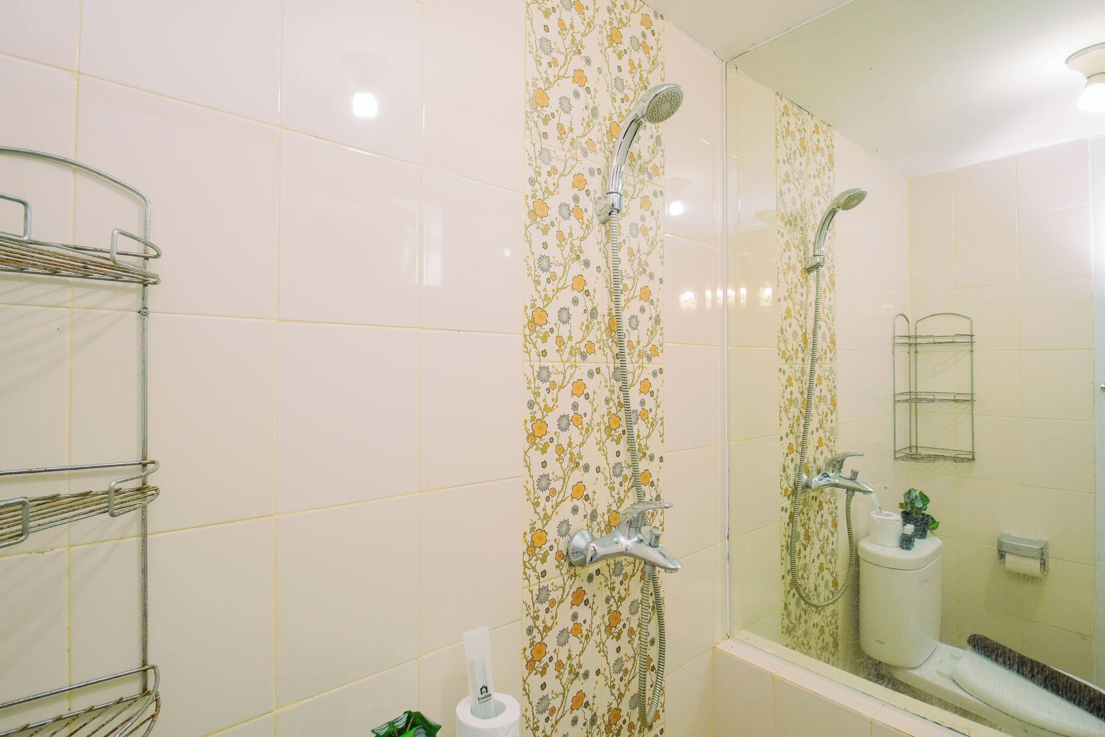 Casa de banho com paredes revestidas a azulejos brancos, chuveiro com padrão floral, sanita e um porta-toalhas.