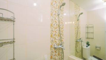Casa de banho com paredes revestidas a azulejos brancos, chuveiro com padrão floral, sanita e um porta-toalhas.