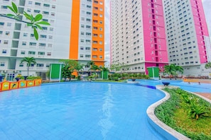 Piscina cercada por vegetação e edifícios residenciais altos.