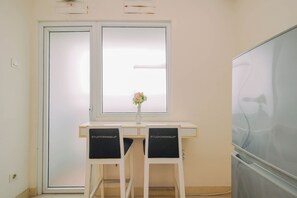 Quarto com escrivaninha branca, duas cadeiras, janela com vista e um espelho grande.