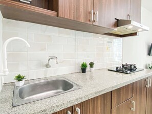 Cozinha com pia de aço inoxidável, backsplash de azulejos brancos, armários de madeira, fogão a gás e duas plantas em vasos.