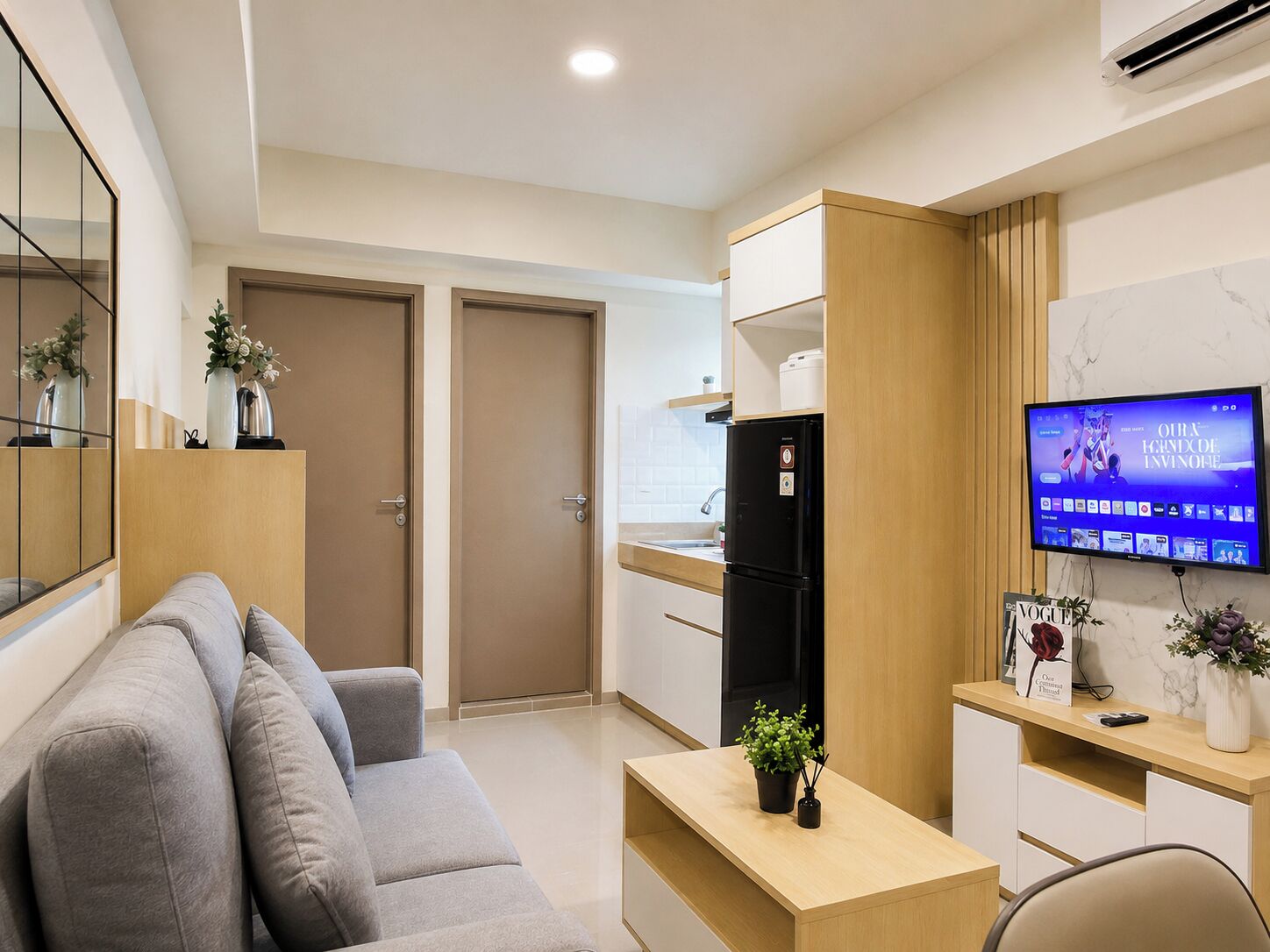 Uma sala de estar moderna com um sofá cinzento, uma mesa de centro de madeira, uma geladeira preta e uma TV de tela plana fixada na parede.