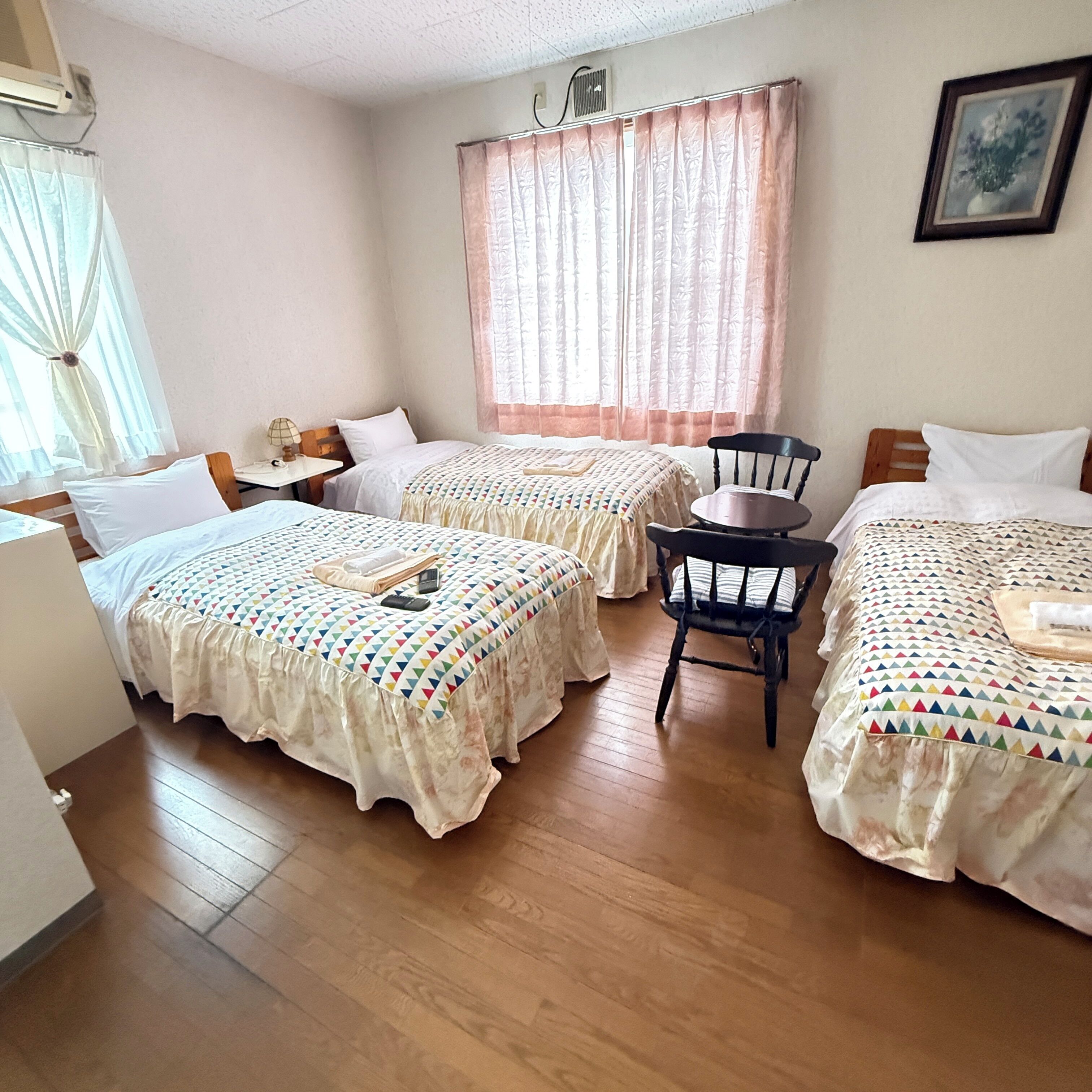 Quarto de hotel com duas camas, uma mesa pequena e uma cadeira.