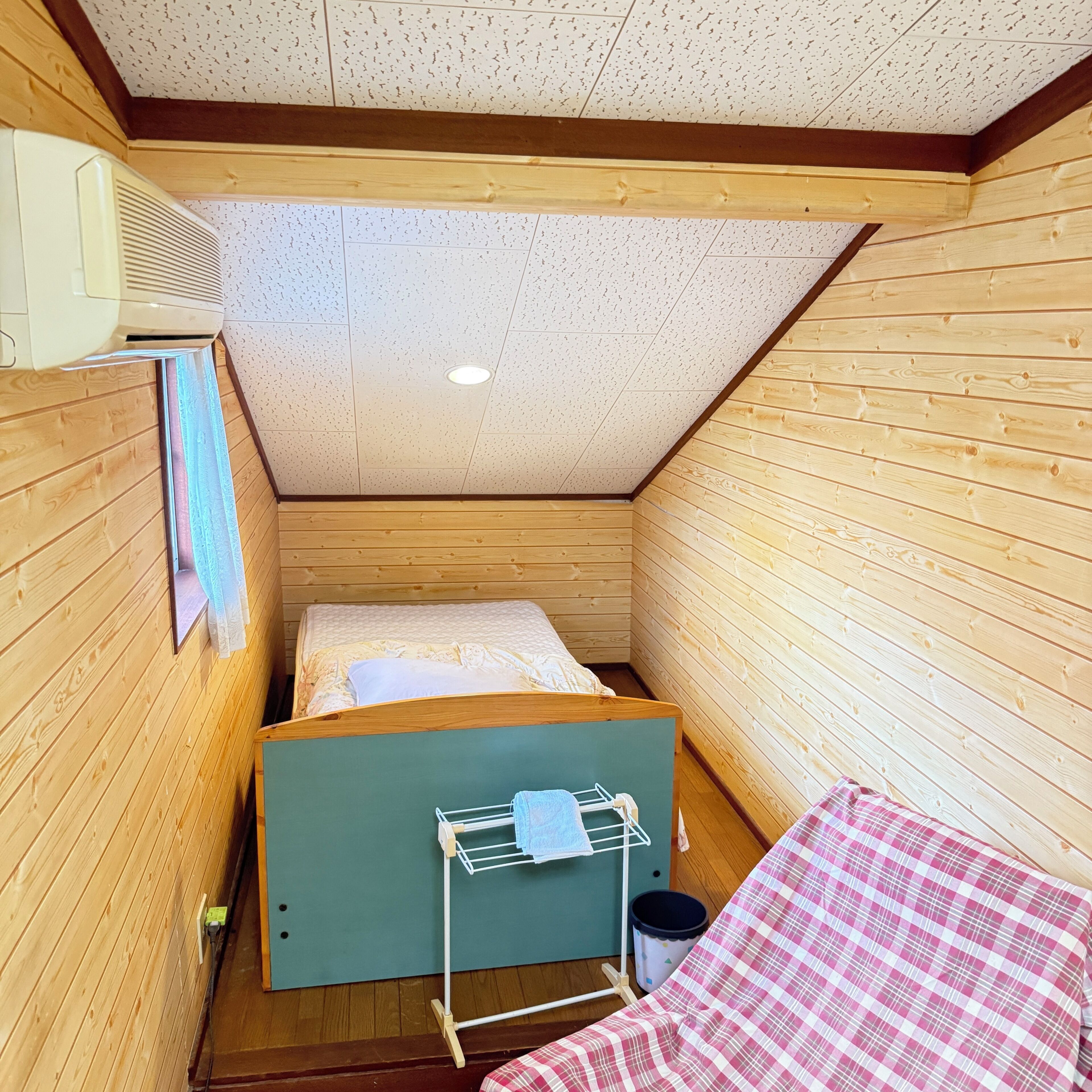 Um quarto pequeno e estreito, com paredes de madeira e teto inclinado.