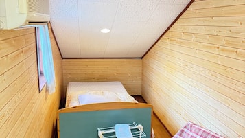 Um quarto pequeno e estreito, com paredes de madeira e teto inclinado.