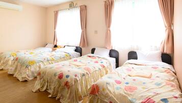 Quarto de hotel com três camas, cada uma com roupa de cama floral, uma mesa de cabeceira com abajur e uma janela com cortinas.