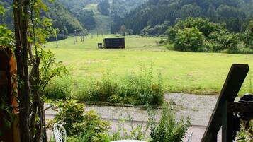 Um pátio com jardim, com cadeiras e mesa brancas, com vista para um campo gramado e um edifício distante.