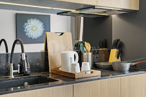 Cozinha moderna com bancada preta, eletrodomésticos de aço inoxidável e tábua de corte de madeira com utensílios.