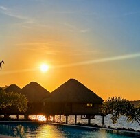 Resort com bangalôs sobre a água, piscina e vista para o pôr do sol.