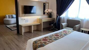 Quarto de hotel com cama, escrivaninha, cadeira, televisão e janela com cortinas.