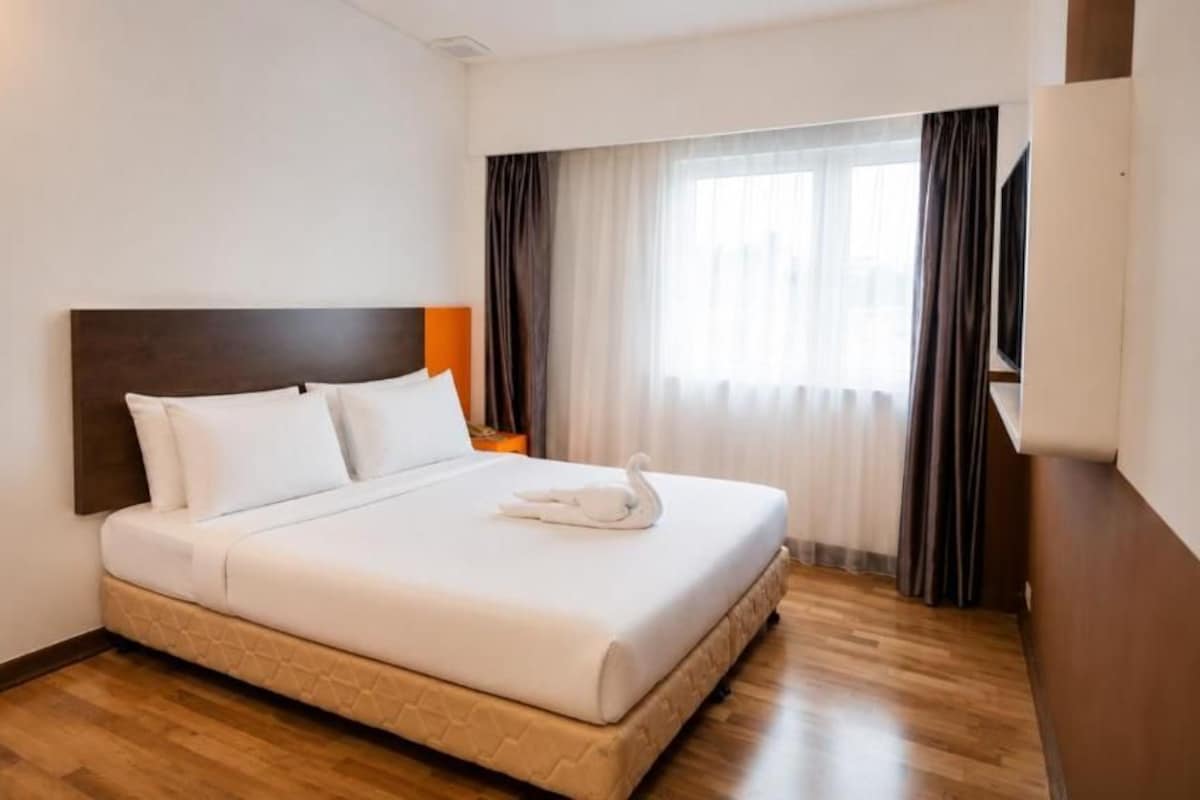 Quarto de hotel com cama, cortinas, televisão e piso de madeira.