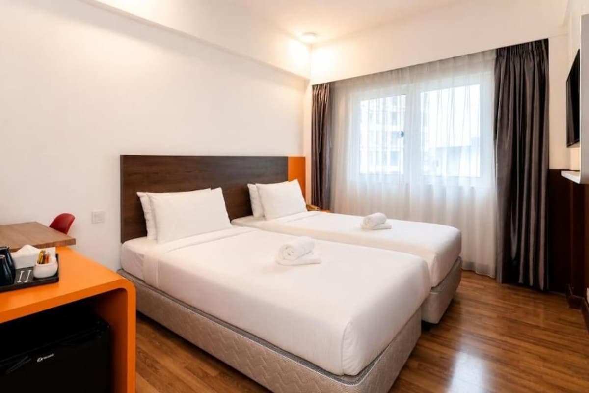 Quarto de hotel com duas camas, uma mesa de trabalho com cafeteira e televisão na parede.