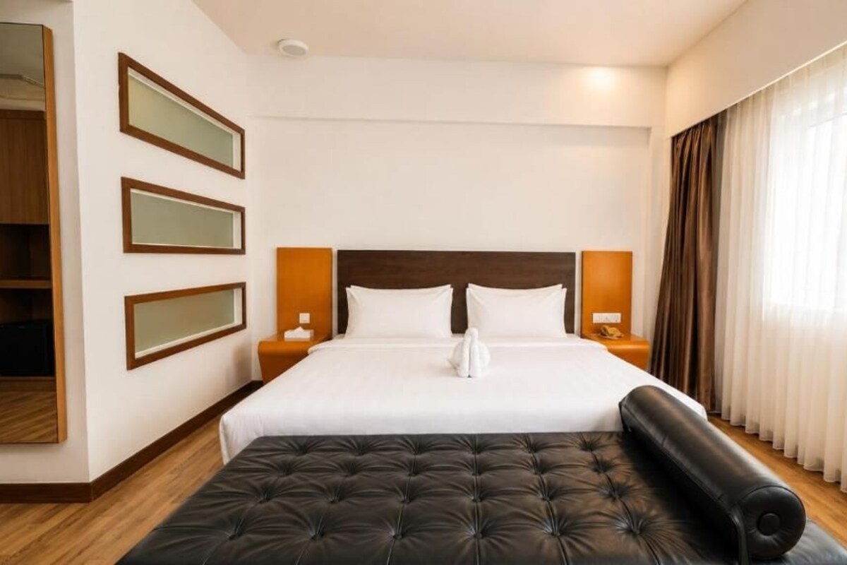 Quarto de hotel com uma cama grande, mesas de cabeceira, um guarda-roupa e uma janela com cortinas.