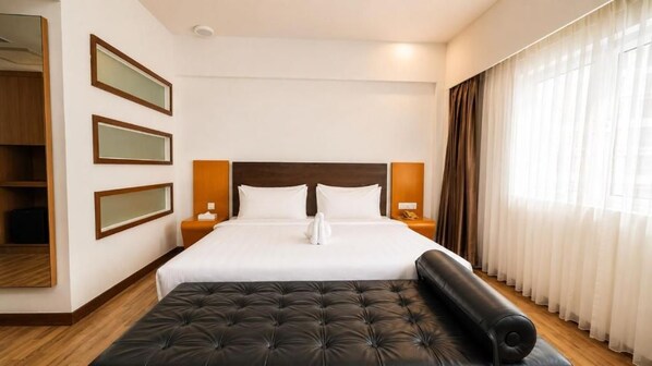 Quarto de hotel com uma cama grande, mesas de cabeceira, um guarda-roupa e uma janela com cortinas.