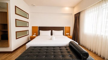 Quarto de hotel com uma cama grande, mesas de cabeceira, um guarda-roupa e uma janela com cortinas.