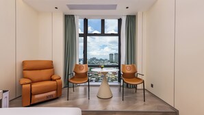 Quarto de hotel com sofá, duas cadeiras, mesa pequena e vista para a paisagem urbana através de amplas janelas.