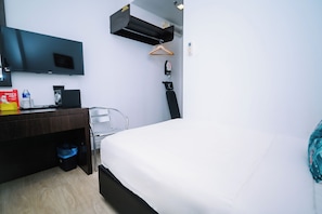 Quarto de hotel com cama, escrivaninha com computador, televisão e cabideiro.