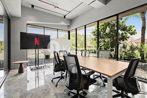Uma sala de conferências moderna com uma mesa grande, cadeiras de escritório pretas e uma tela de TV exibindo o logotipo da Netflix.
