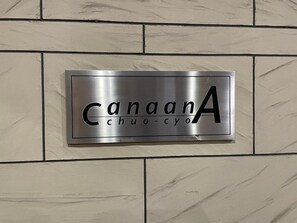 Uma placa metálica com os textos 'Canaan' e 'chuo-cyo' em uma parede azulejada.