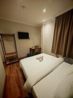 Quarto de hotel com cama, escrivaninha, cadeira, televisão e janela com cortinas.