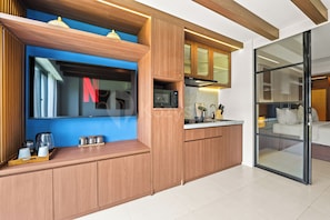 Uma cozinha moderna com armários de madeira, micro-ondas embutido e divisória de vidro que dá para um quarto.