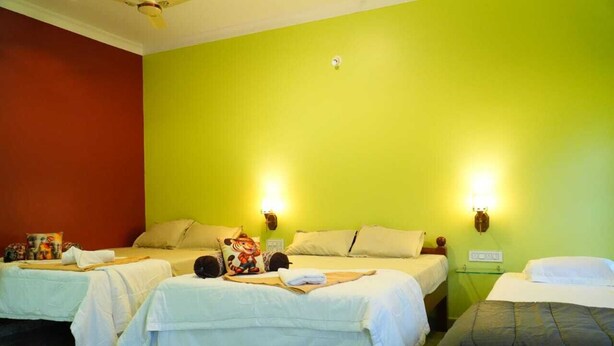 Quarto de hotel com duas camas, uma parede verde e duas luminárias fixadas na parede.