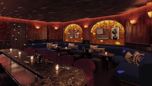 Uma área de bar com pouca luz, assentos, balcão de mármore e luminárias fixadas na parede.