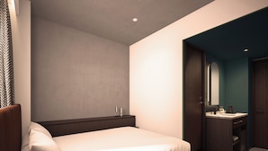 Quarto de hotel moderno com uma cama de solteiro, uma pequena mesa de cabeceira, armário embutido e banheiro com espelho e pia.