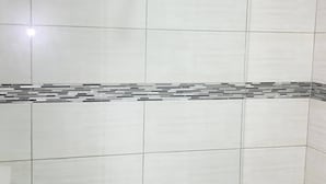 Um banheiro com chuveiro, paredes revestidas de azulejos e ralo.
