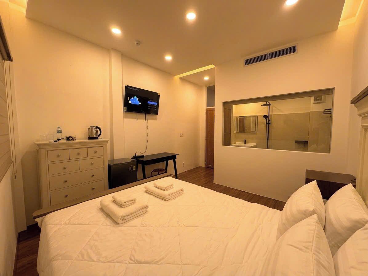 Quarto de hotel com cama, escrivaninha, televisão, espelho e chuveiro.