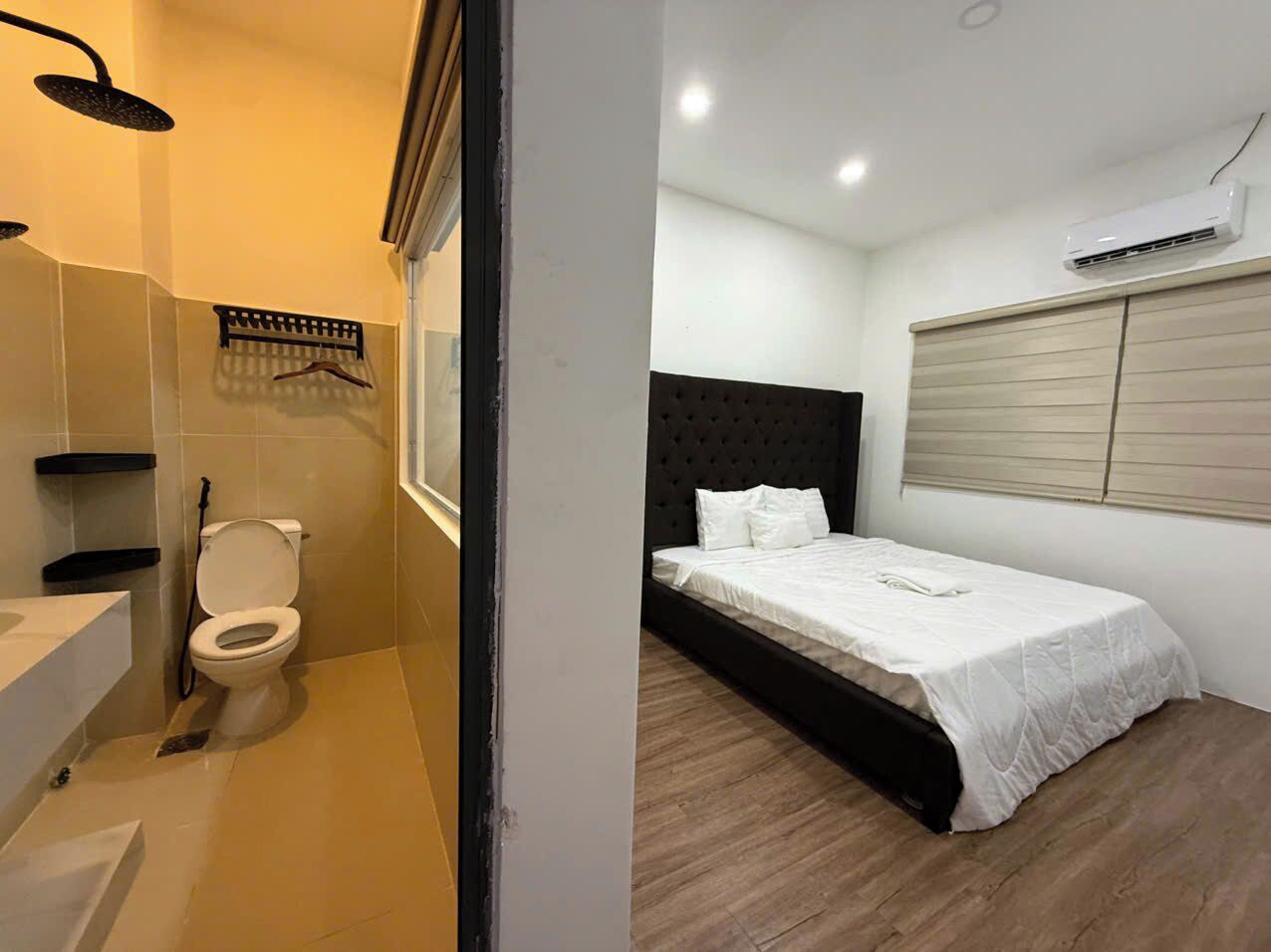 Casa de banho com sanita, chuveiro e cama com cabeceira e janela.