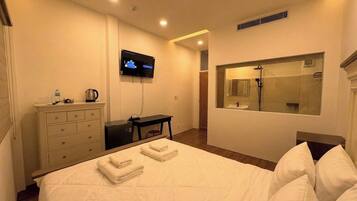 Quarto de hotel com cama, escrivaninha, televisão, banheiro com espelho e TV fixada na parede.