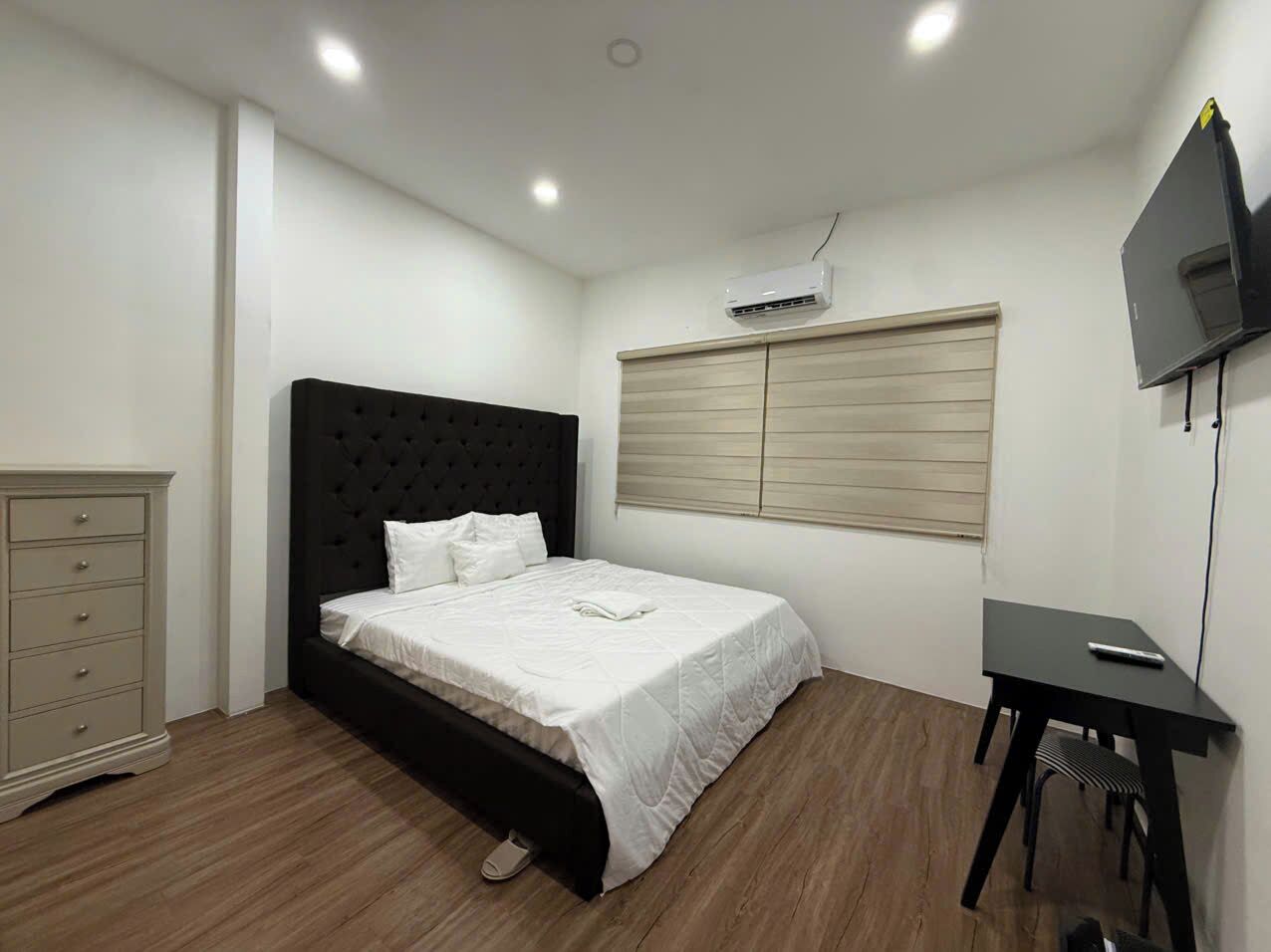 Quarto com cama, cômoda, escrivaninha e televisão.