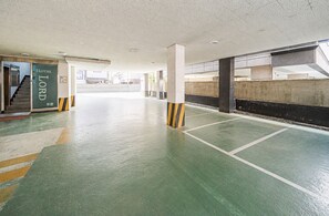 Uma garagem com pilares de concreto, piso verde e placa indicando o Hotel 5.
