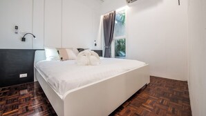 Quarto de hotel com uma cama grande, janela com cortinas, aparelho de ar condicionado e luminária fixa na parede.