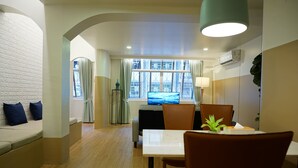 Quarto de hotel com área de refeições, sofá com almofadas, mesa com cadeiras e uma grande janela com cortinas.