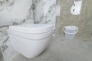Um banheiro moderno com vaso sanitário branco, parede de mármore e uma pequena lixeira.