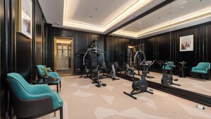 Sala de ginástica com equipamentos de exercício, cadeiras cor verde-água e um espelho grande.