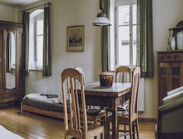 Um quarto com uma mesa de jantar de madeira, cadeiras, um sofá, um radiador e uma janela com cortinas.
