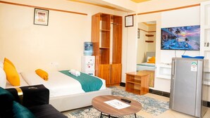 Quarto de hotel com cama, sofá, uma pequena mesa, frigorífico, dispensador de água, televisão e um quadro na parede.