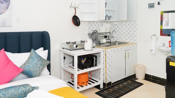Quarto de hotel compacto com cama, bancada de cozinha e banheiro pequeno.