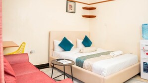 Quarto de hotel com uma cama, uma cadeira vermelha, uma mesa pequena e um dispensador de água.
