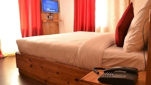 Uma cama com cabeceira de madeira, uma televisão presa a uma prateleira de madeira e um telefone em uma mesinha de cabeceira de madeira.