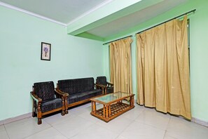 Sala de estar com sofá, mesa de centro de vidro e cortinas bege.