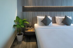 Quarto de hotel moderno com cama, mesas de cabeceira, planta em vaso e luminária na parede.