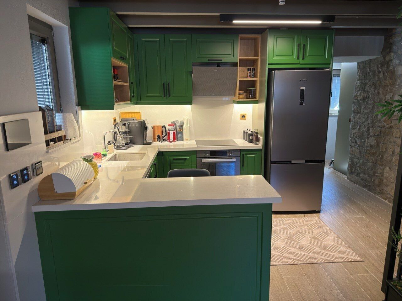 Cozinha moderna com armários verdes, eletrodomésticos de aço inoxidável e uma ilha central.