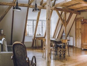 A rustic room with exposed wooden beams, a dining table with chairs, and a window with a view of trees.